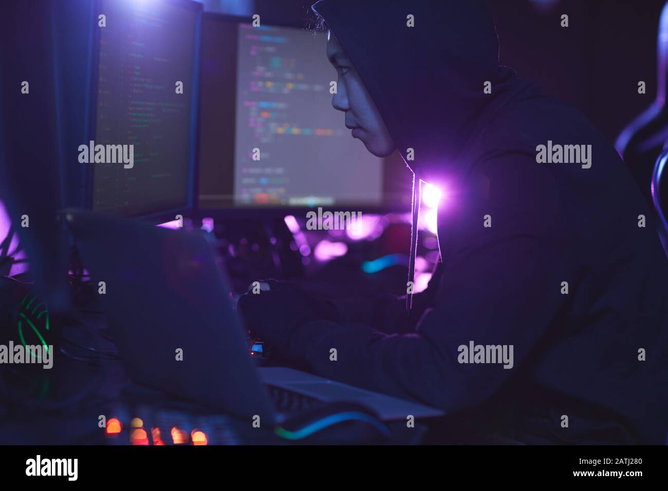 Side view at unrecognizable cyber security hacker wearing hood while working on programming in ...