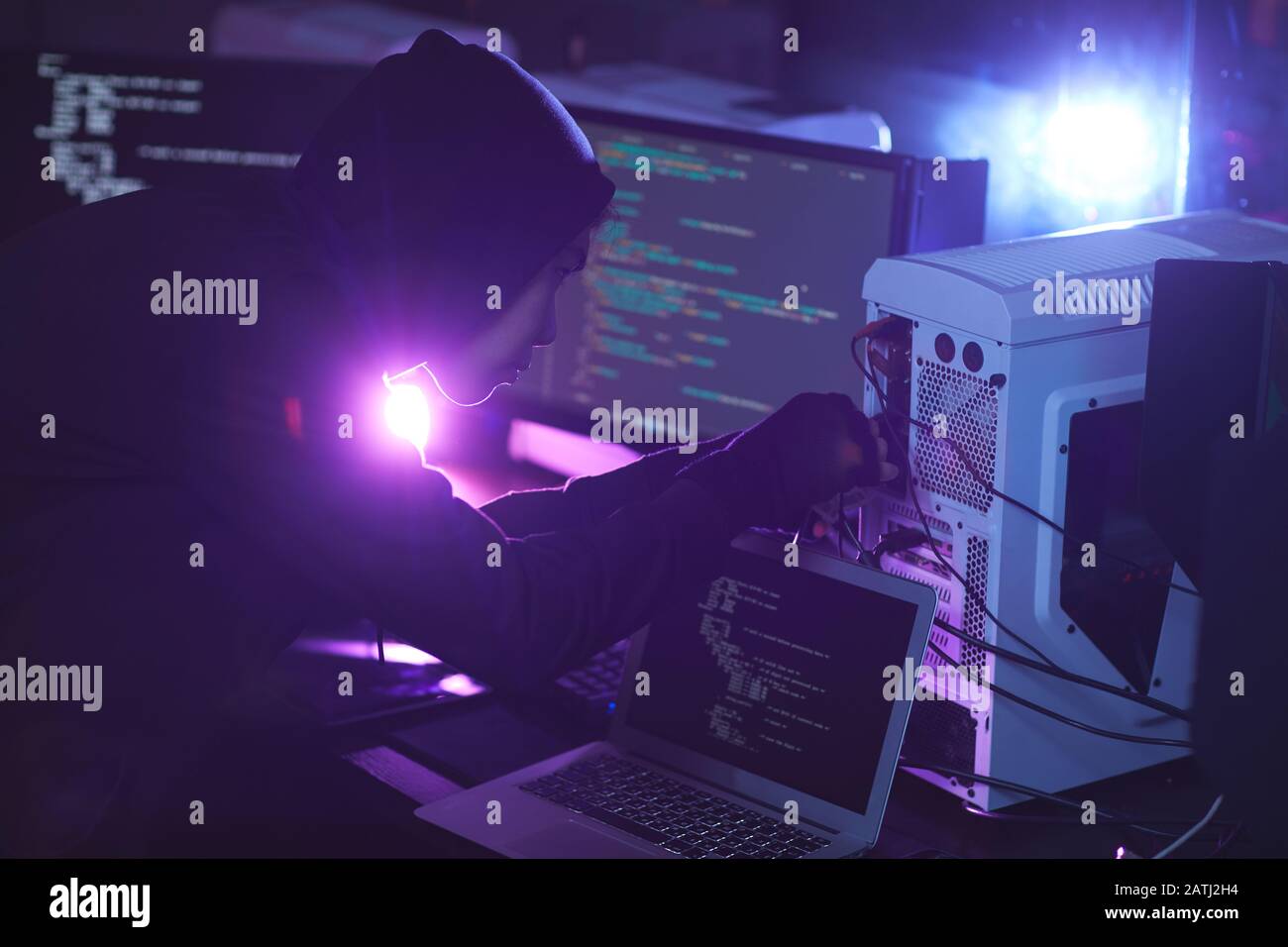 Side view at unrecognizable cyber security hacker wearing hood while working on computer system ...