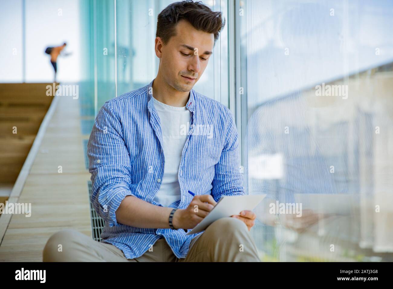 Man writing in notebook, sitting on steps at big windows, big working ...
