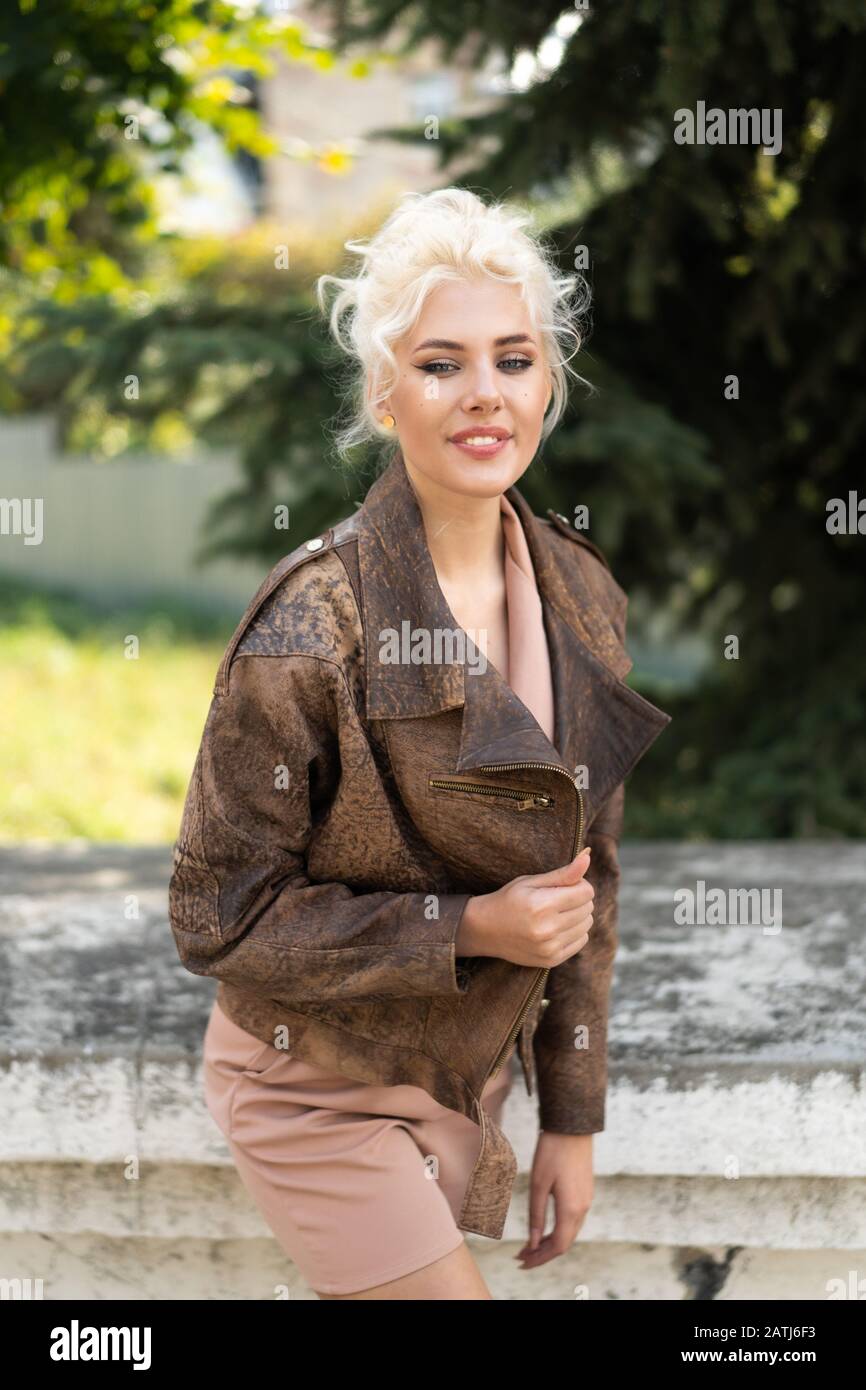 Smiling blonde woman in vintage leather jacket posing on street Stock ...