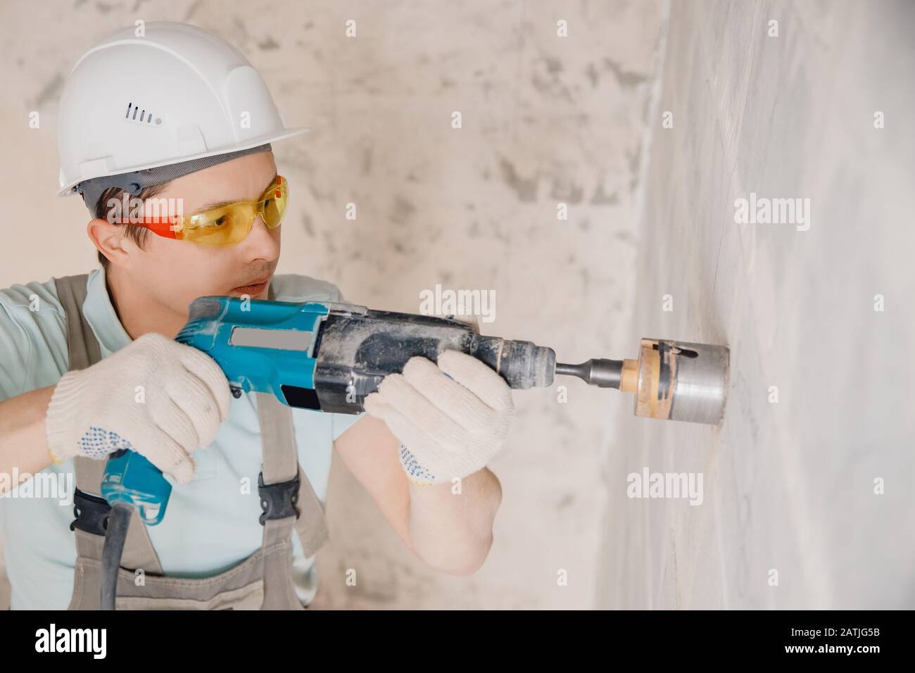Builder man cutting electrical chase in concrete wall with hammer drill ...