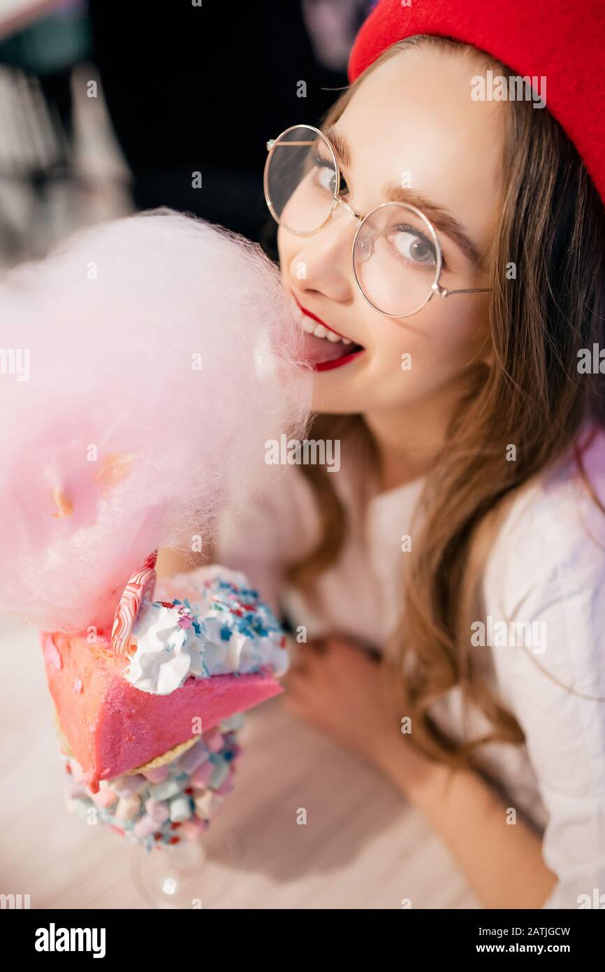 Young woman in red beret and glasses has sweet dessert with candy floss ...