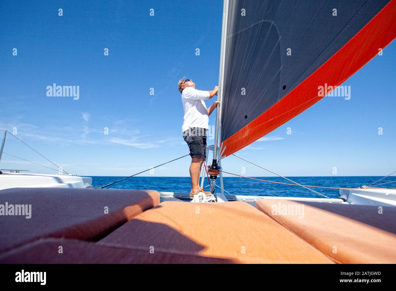 A sailor on the foredeck of a catamaran checking on the rigging during ...