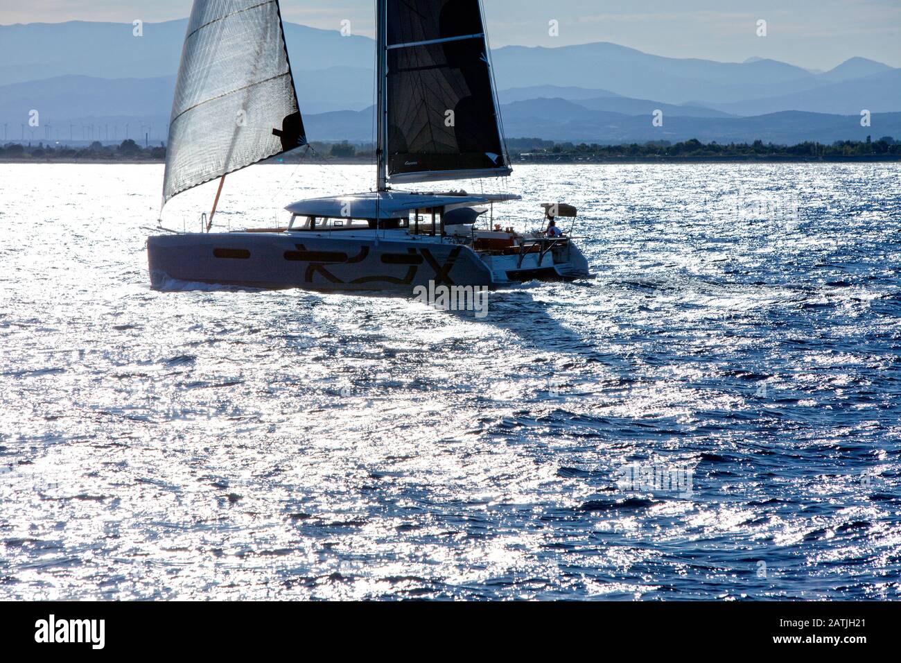 Back light vision of a cruising catamaran under sails by a beautiful ...