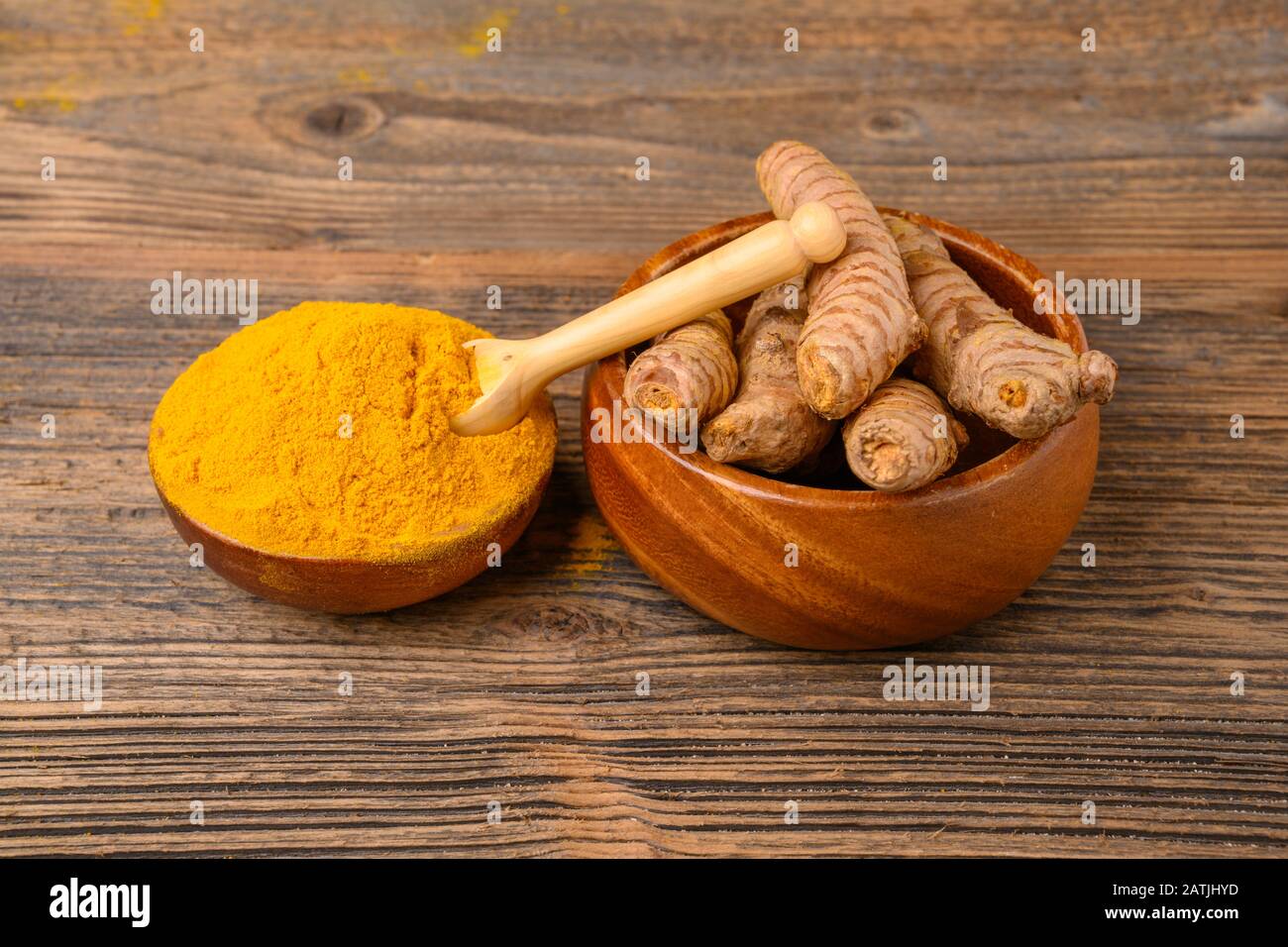 Fresh whole turmeric roots and dried curcuma powder in a wooden bowl in ...