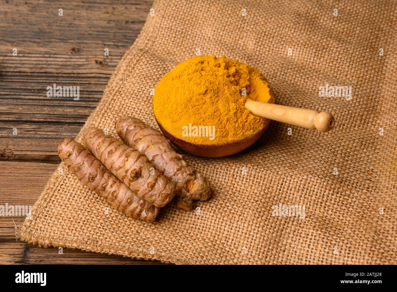 Fresh whole turmeric roots and dried curcuma powder in a wooden bowl ...