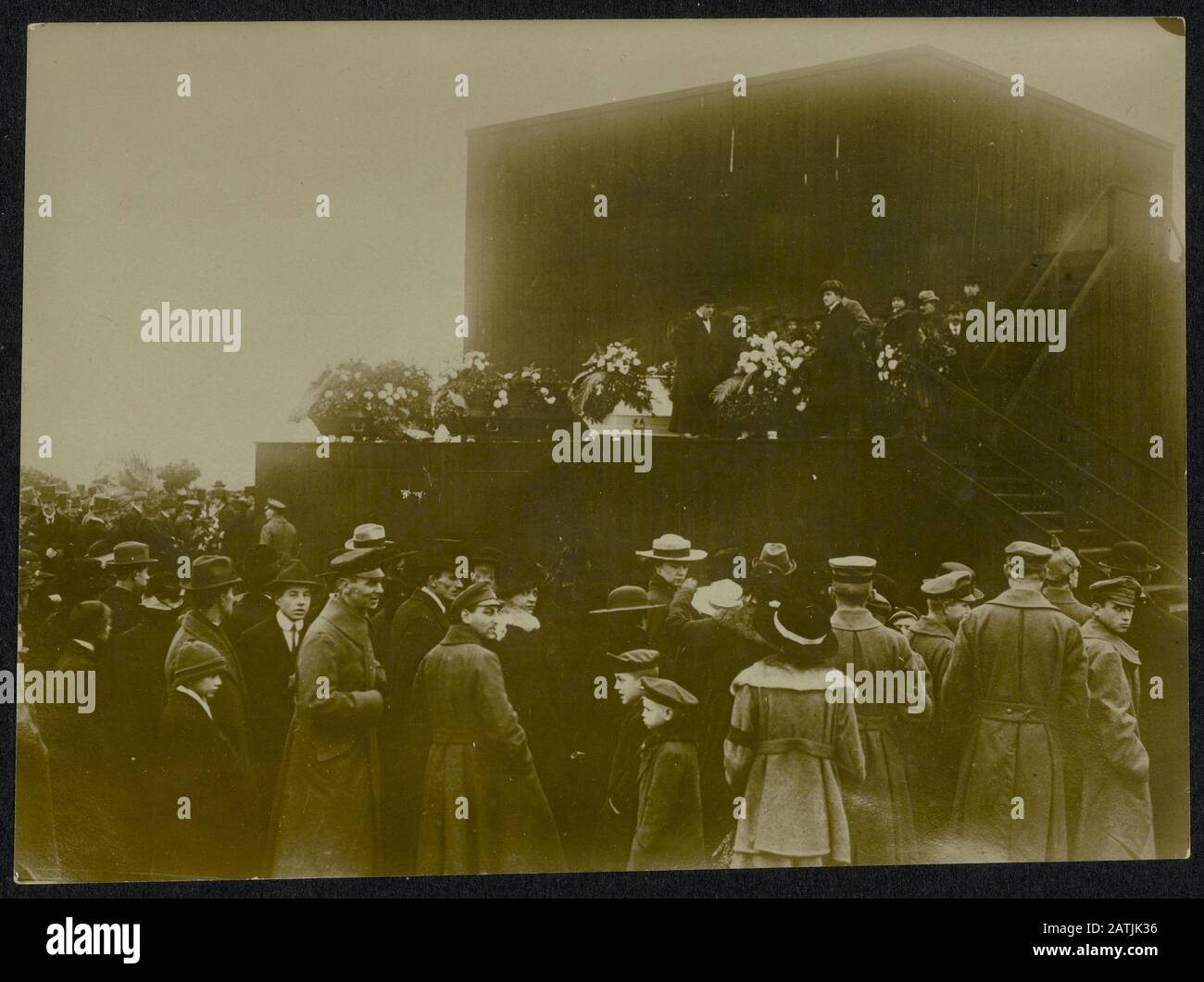 Description: Podium, flower-covered coffins and grieving crowd ...