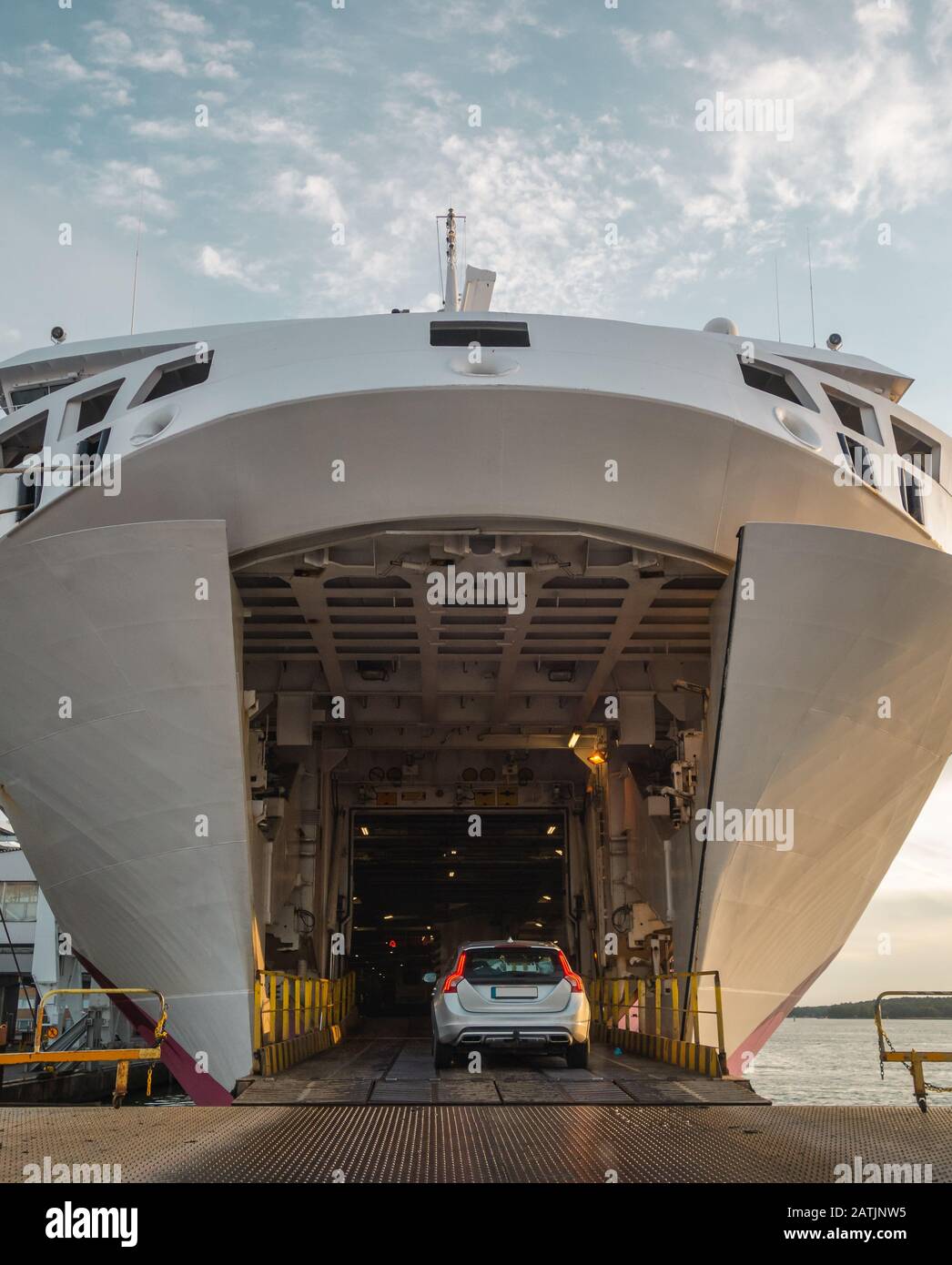 Bow doors are open and cars are driving inside a big car ferry in the ...
