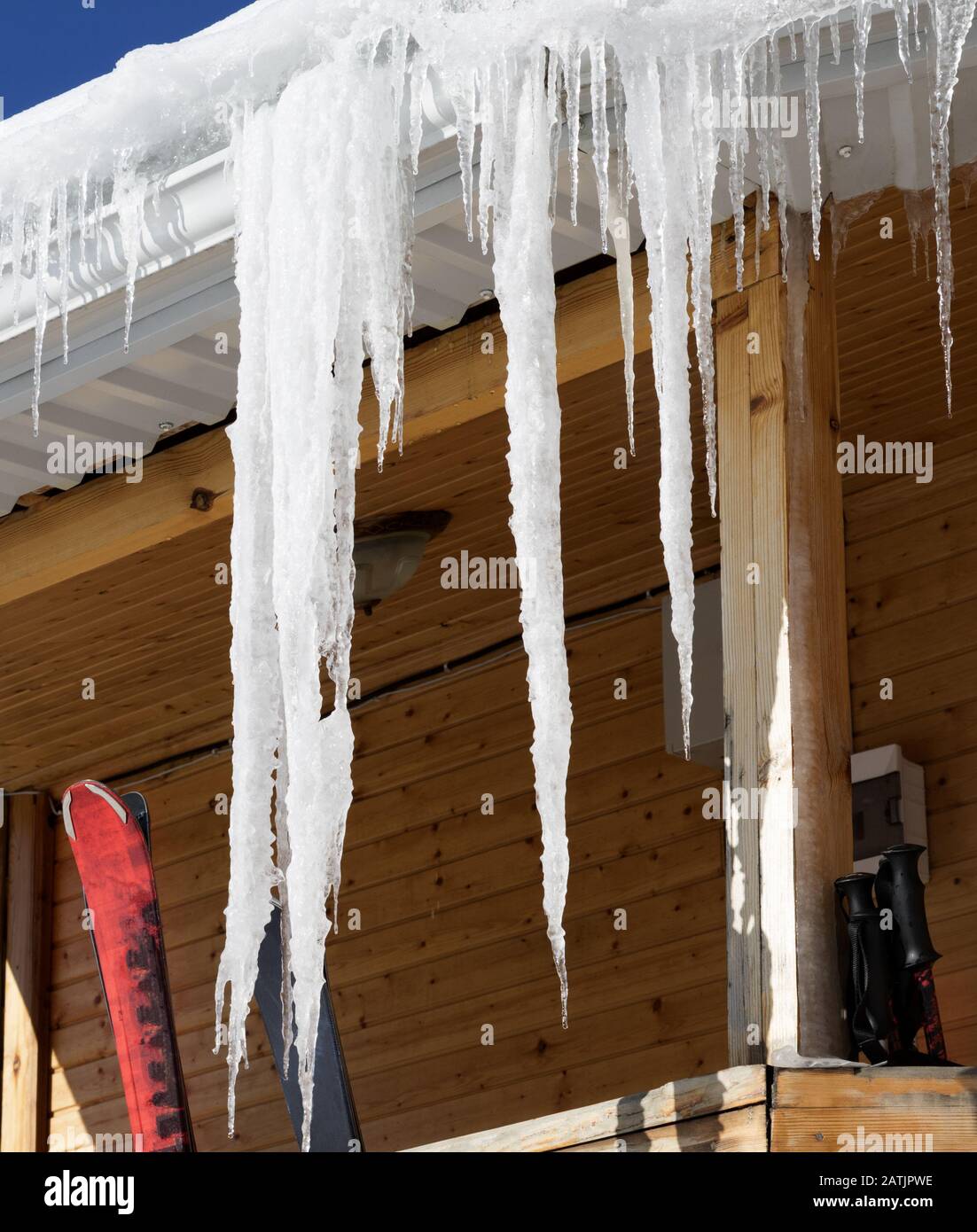Wooden house with snow cornice and big icicles on roof and ski ...