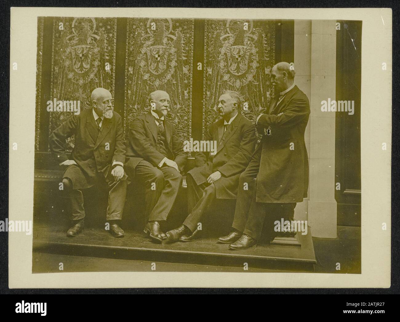 Description: Four men posing in front of a wall decorated with coats of ...