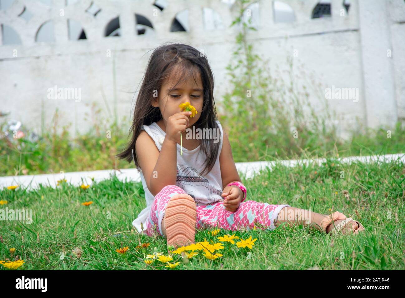 Sad little girl smelling flowers sitting on the grass Stock Photo - Alamy