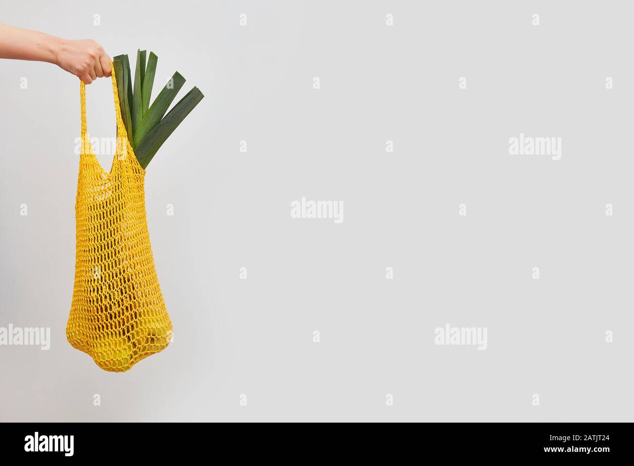 Yellow mesh bag with leek in hand on a gray background with copy space ...