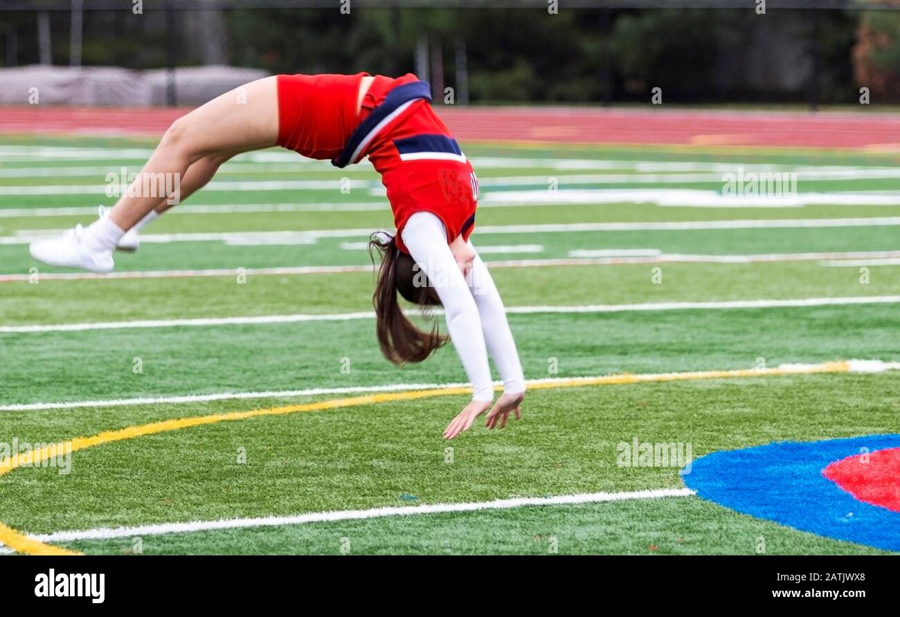 A high school cheerleader is landing on her hands performing flips on a ...