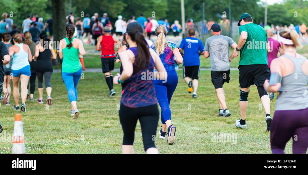 Rear view of male and female runners racing a 10K on a grass field at ...