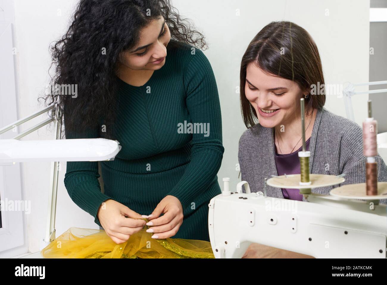Pretty seamstress teaching girl working with sewing machine at sewing ...