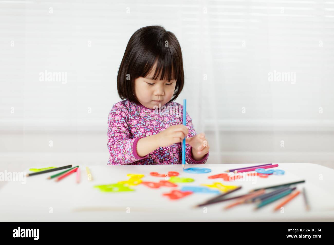 toddler girl practice writing letters on white paper against white ...
