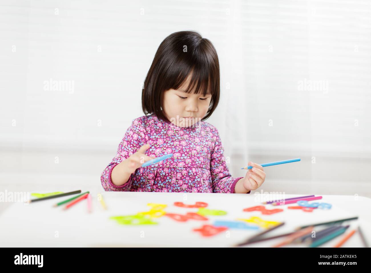toddler girl practice writing letters on white paper against white ...