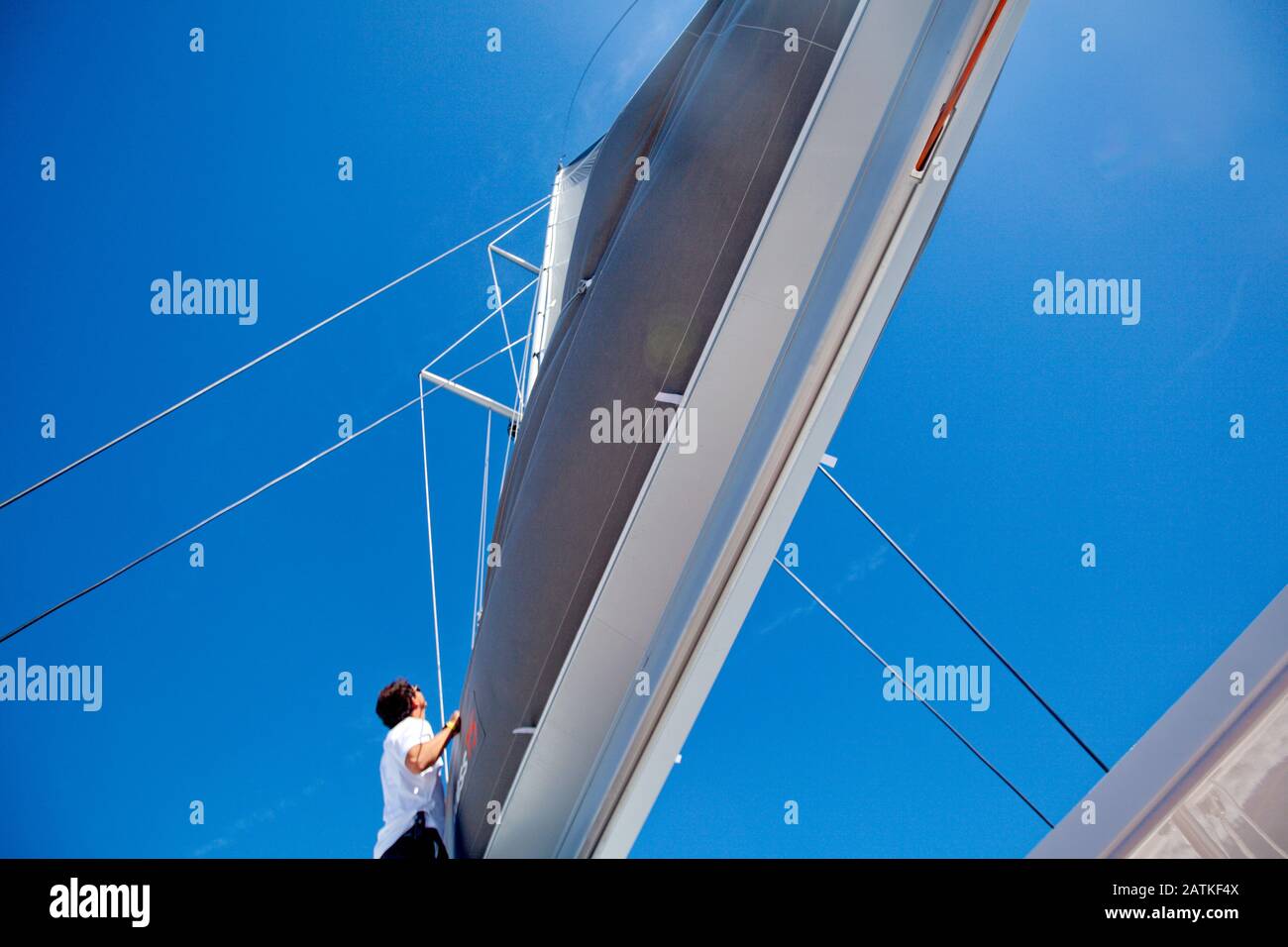 A sailor on the foredeck of a catamaran checking on the rigging during ...