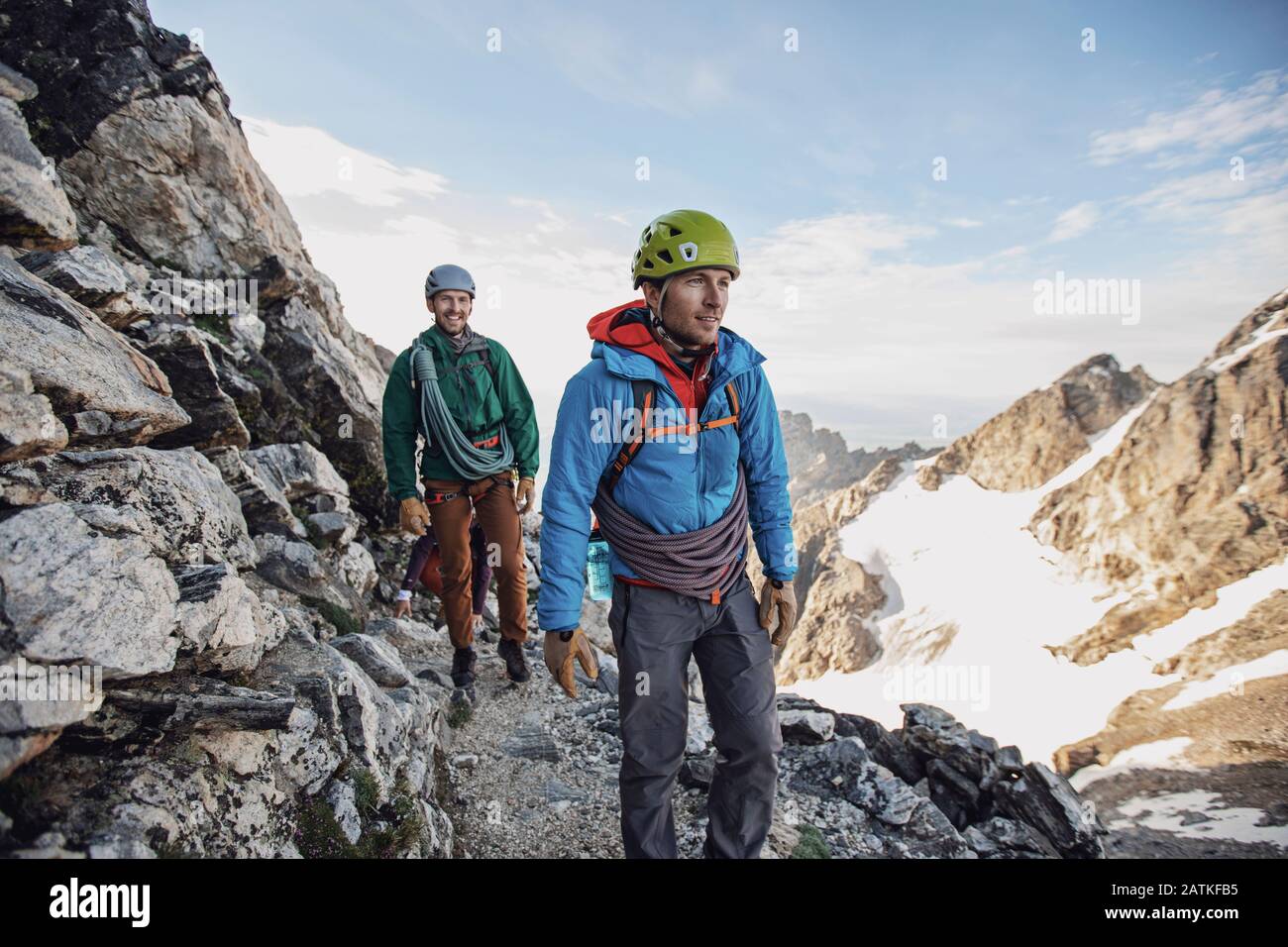 Two rock climbers with helmets and ropes walk along a cliff in Tetons ...