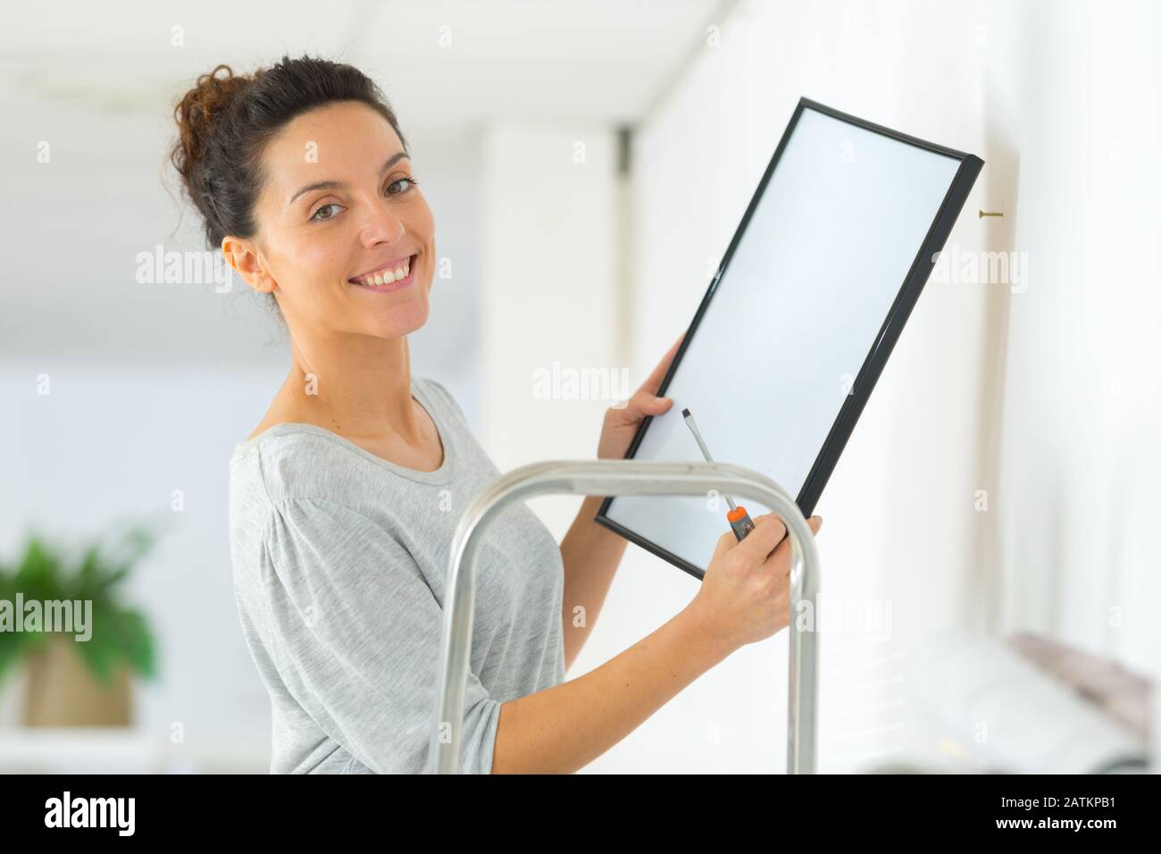 woman positioning picture frame on wall Stock Photo - Alamy