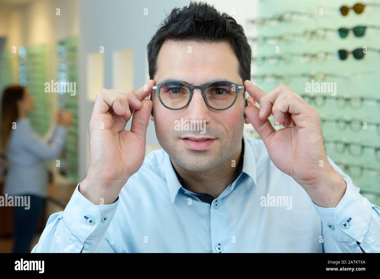 man trying on glasses in optical store while smiling Stock Photo - Alamy