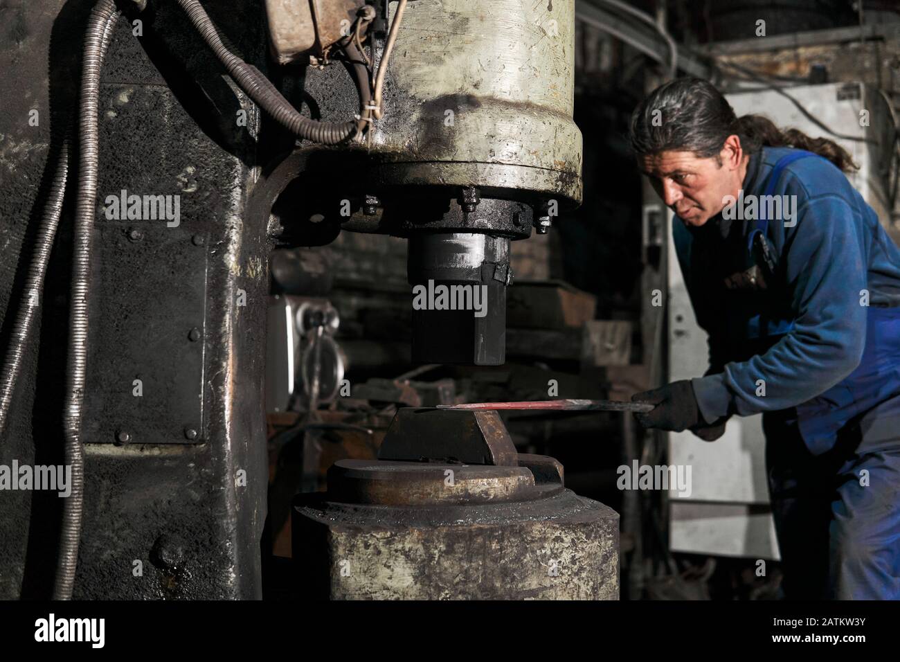 blacksmith processes a hot workpiece with a machine hammer in a ...