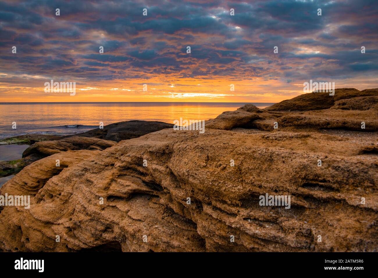 Sandy beach rocks colored in orange under the rays of the rising sun ...