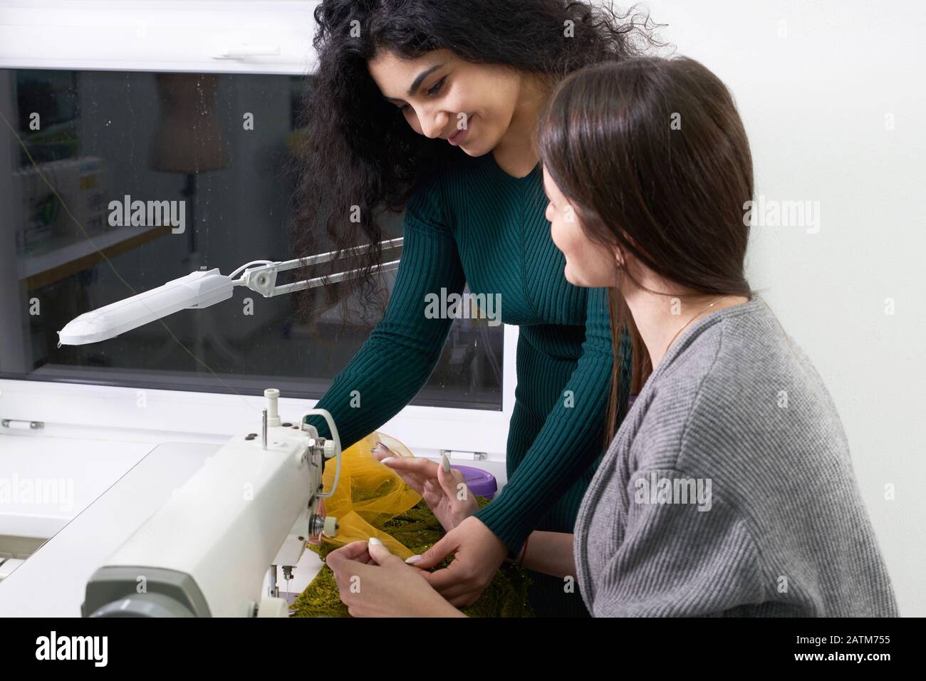 Pretty seamstress teaching girl working with sewing machine at sewing ...