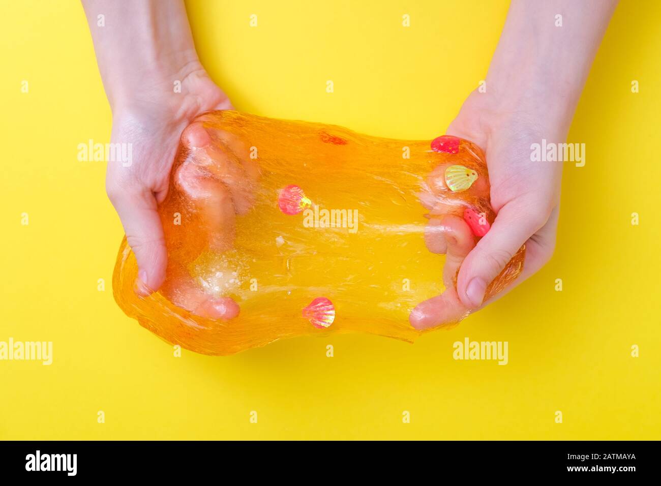 Girl stretching colorful orange slime to the sides. Kids hands playing ...