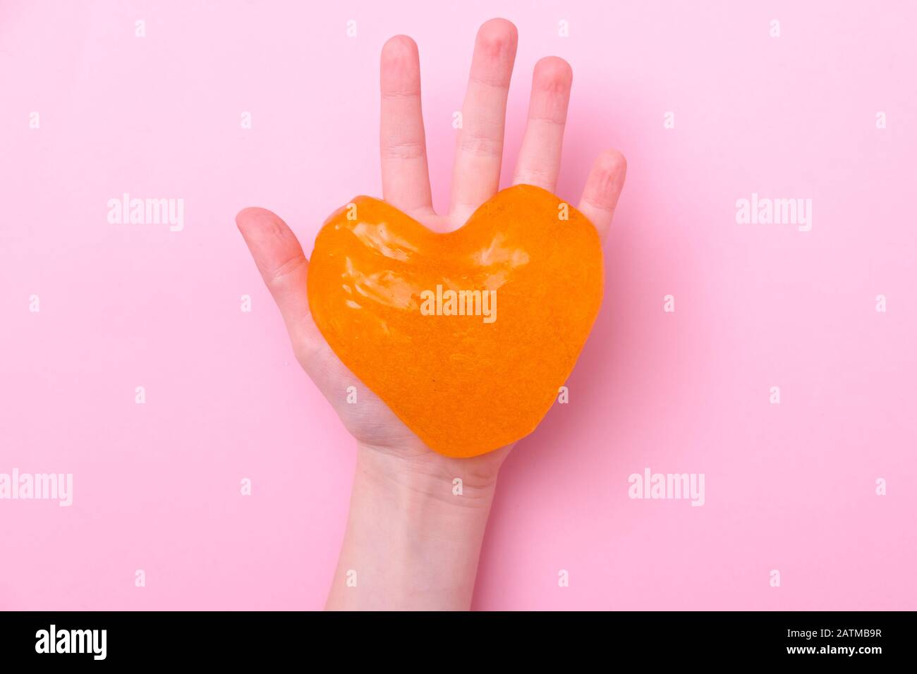 Orange slime in heart shape in kid hands. Girl hands playing slime toy ...