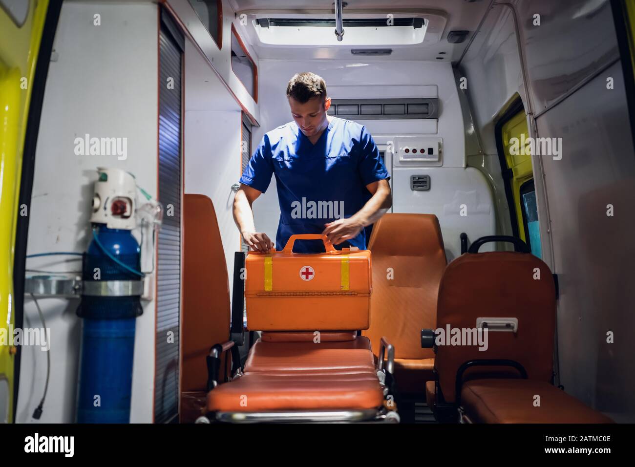 Young doctor in blue medical uniform packs medical bag in the ambulance ...