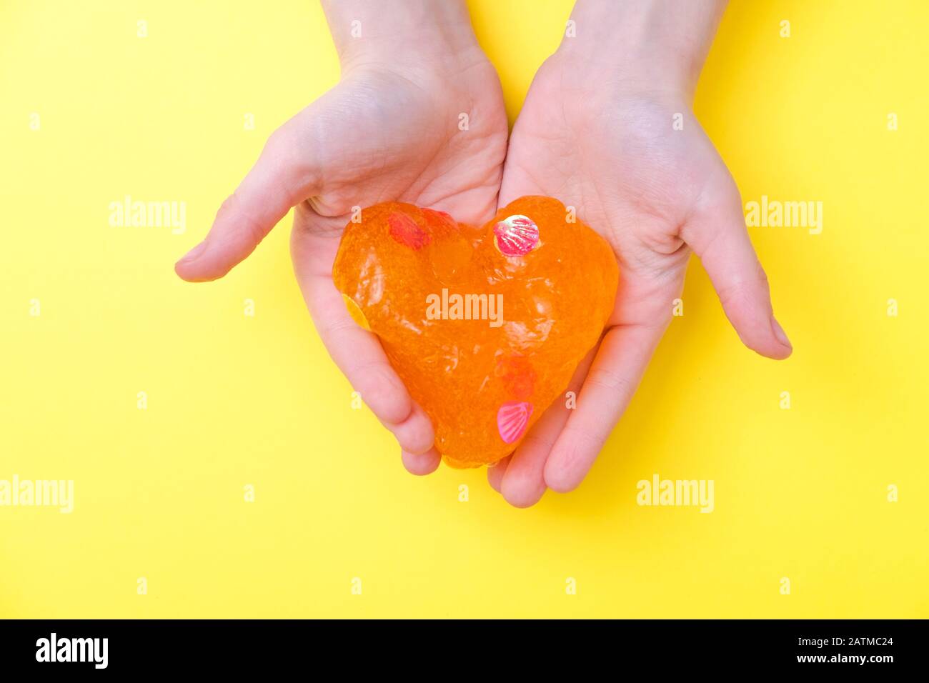 Orange slime in heart shape in kid hands. Girl hands playing slime toy ...