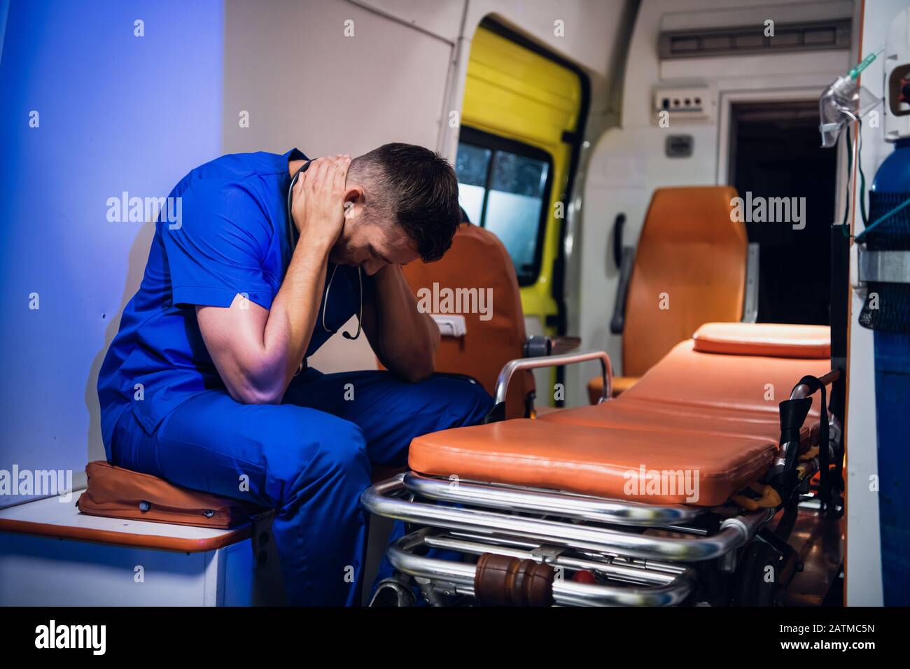 Tired corpsman in uniform sits inside the ambulance car and puts his ...