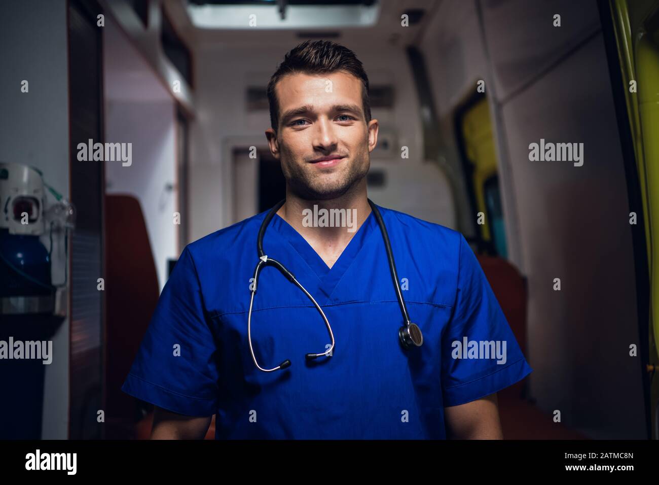Corpsman in blue medical uniform stands with smile in the ambulance car ...