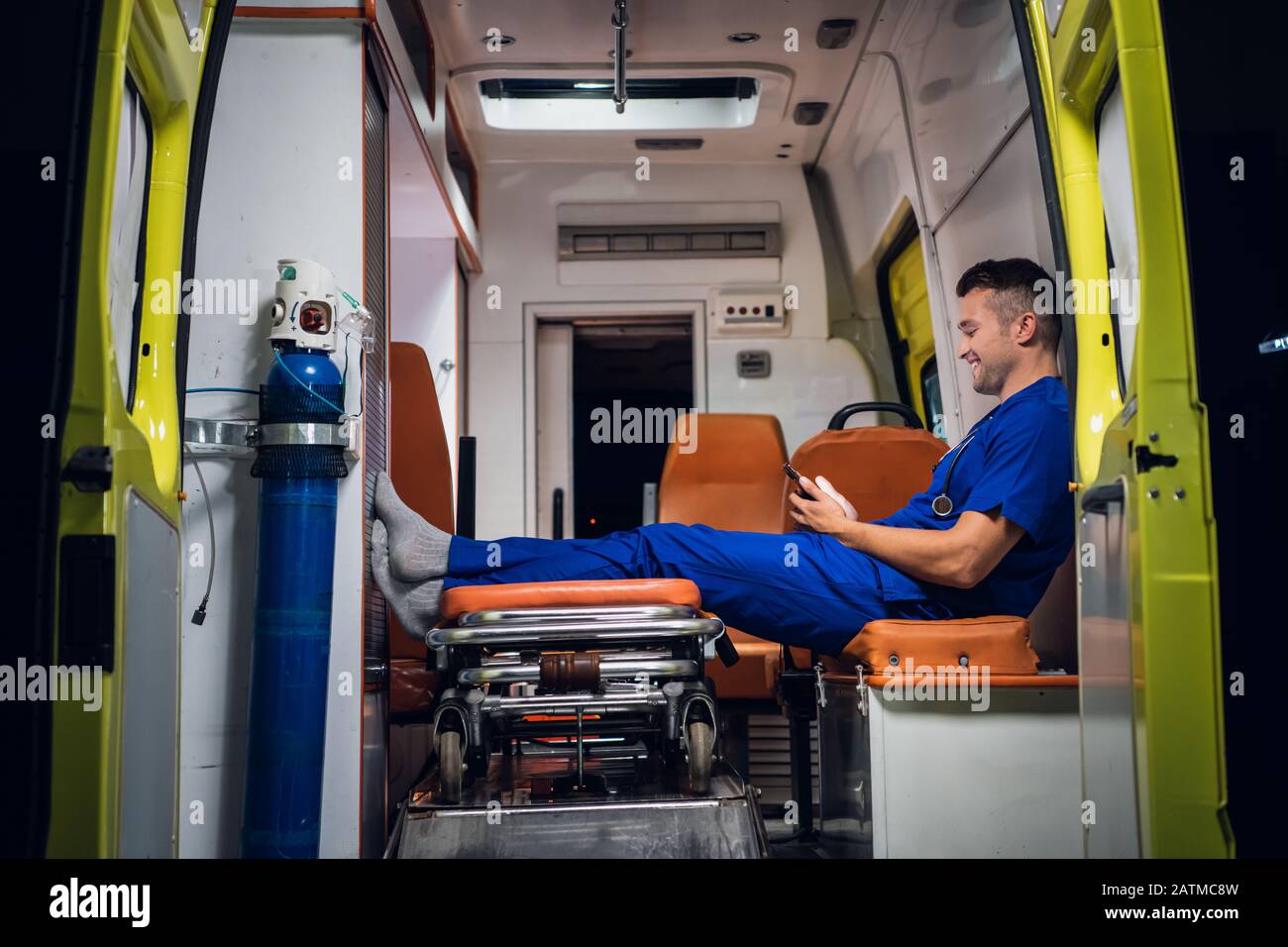 Young paramedic in blue medical uniform sits with phone in his hands in ...