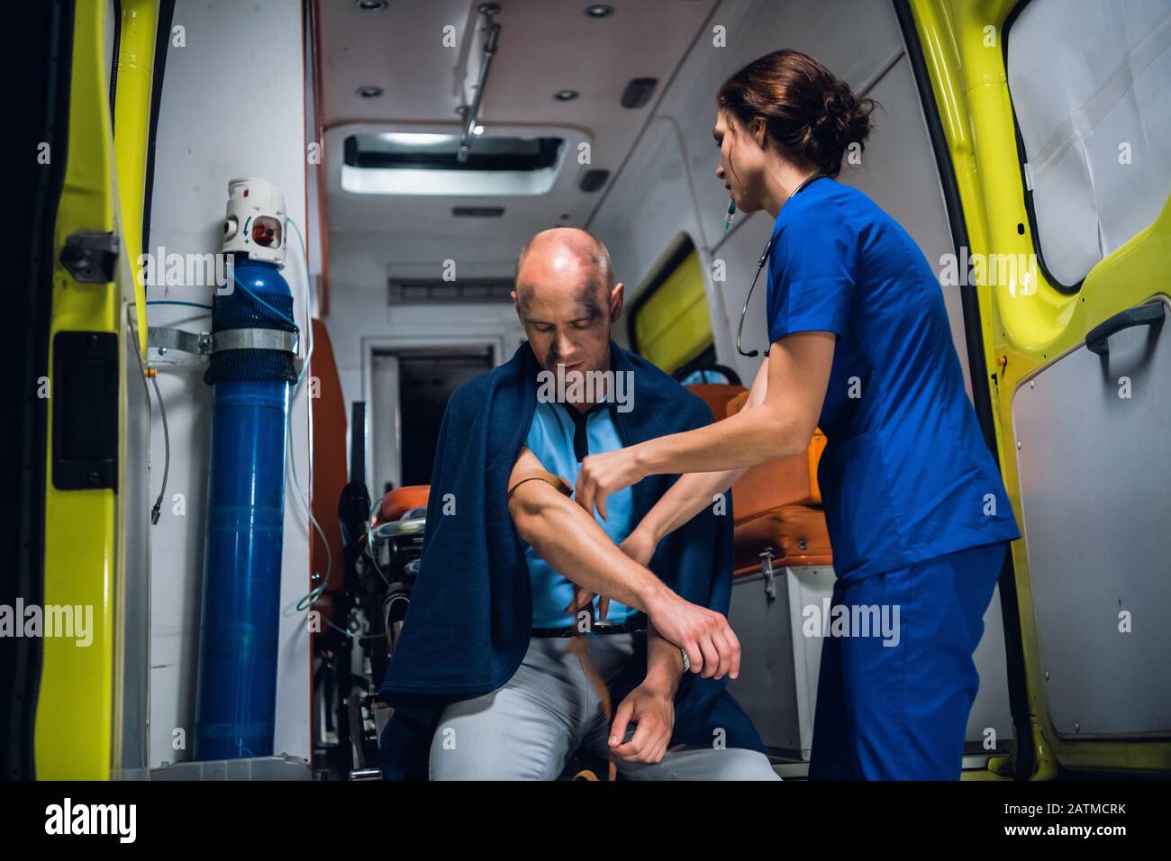 Pretty nurse in medical uniform wraps a tourniquet around a hand of man ...