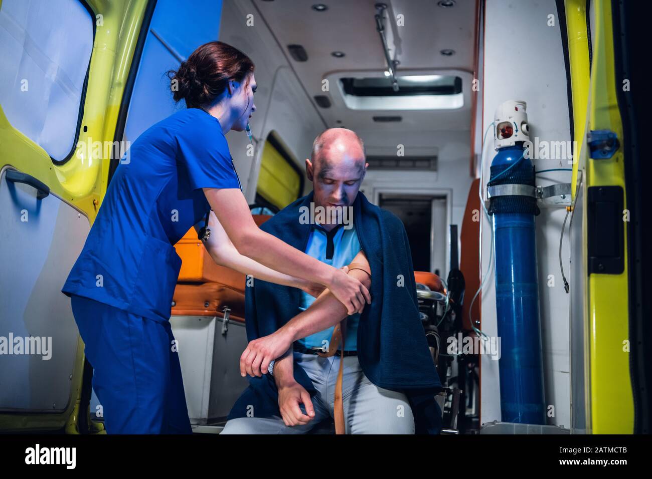 Young nurse in medical uniform wraps a tourniquet around a hand of man ...