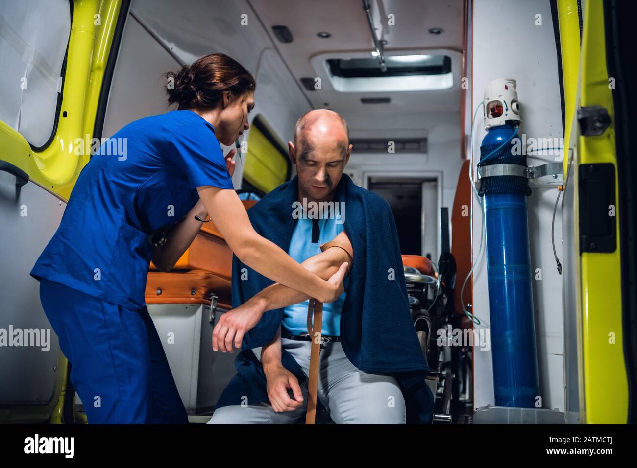 Woman in blue medical uniform wraps a tourniquet around a hand of man ...