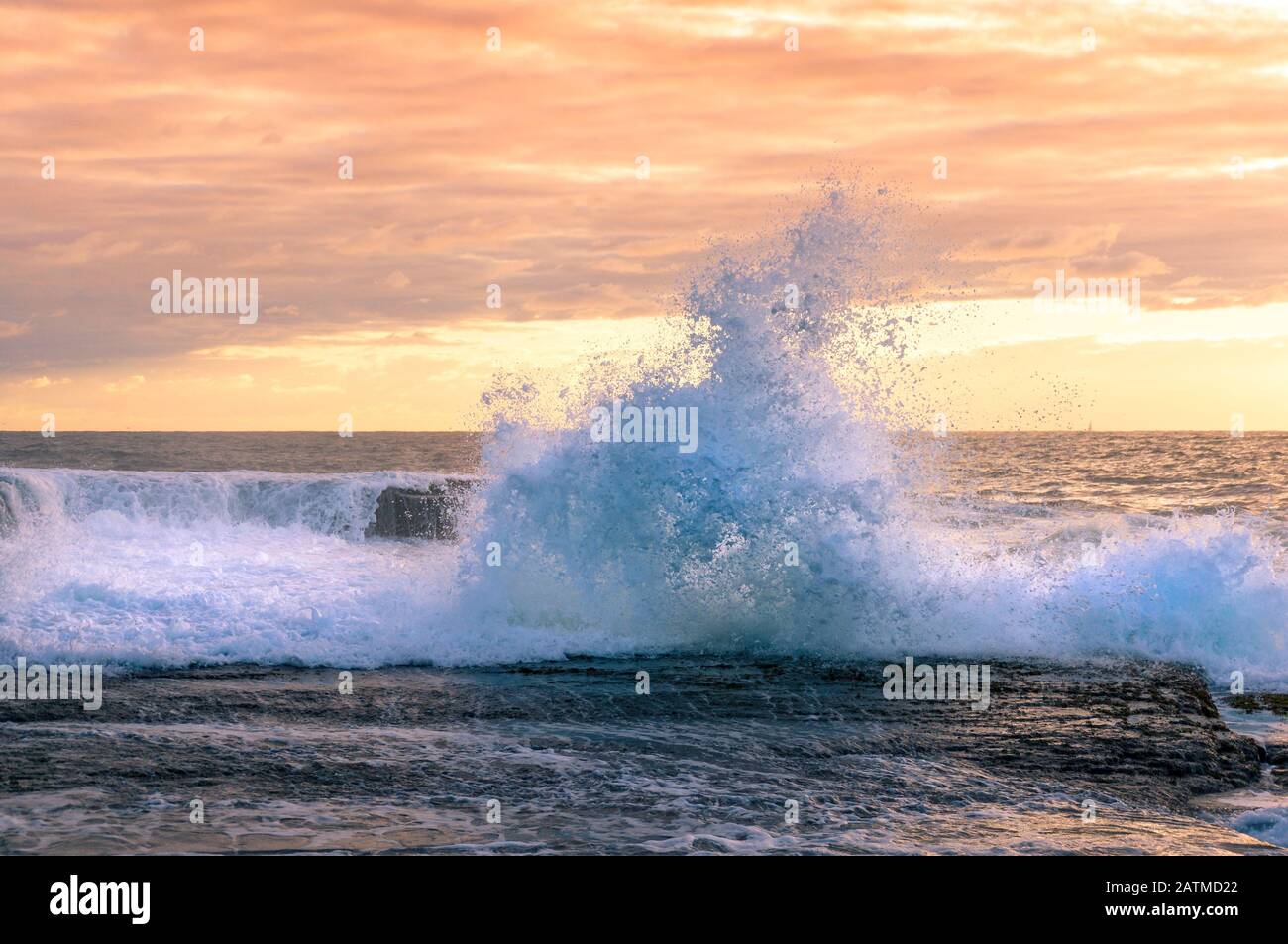 Strong big wave crushing over rocks with beautiful sunset sky on the ...