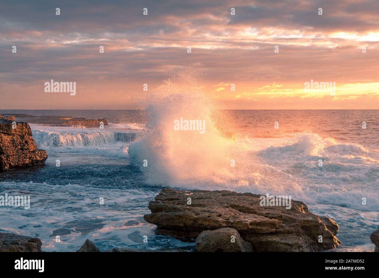 Huge wave crushing over rock with splashes of white foam at sunrise ...