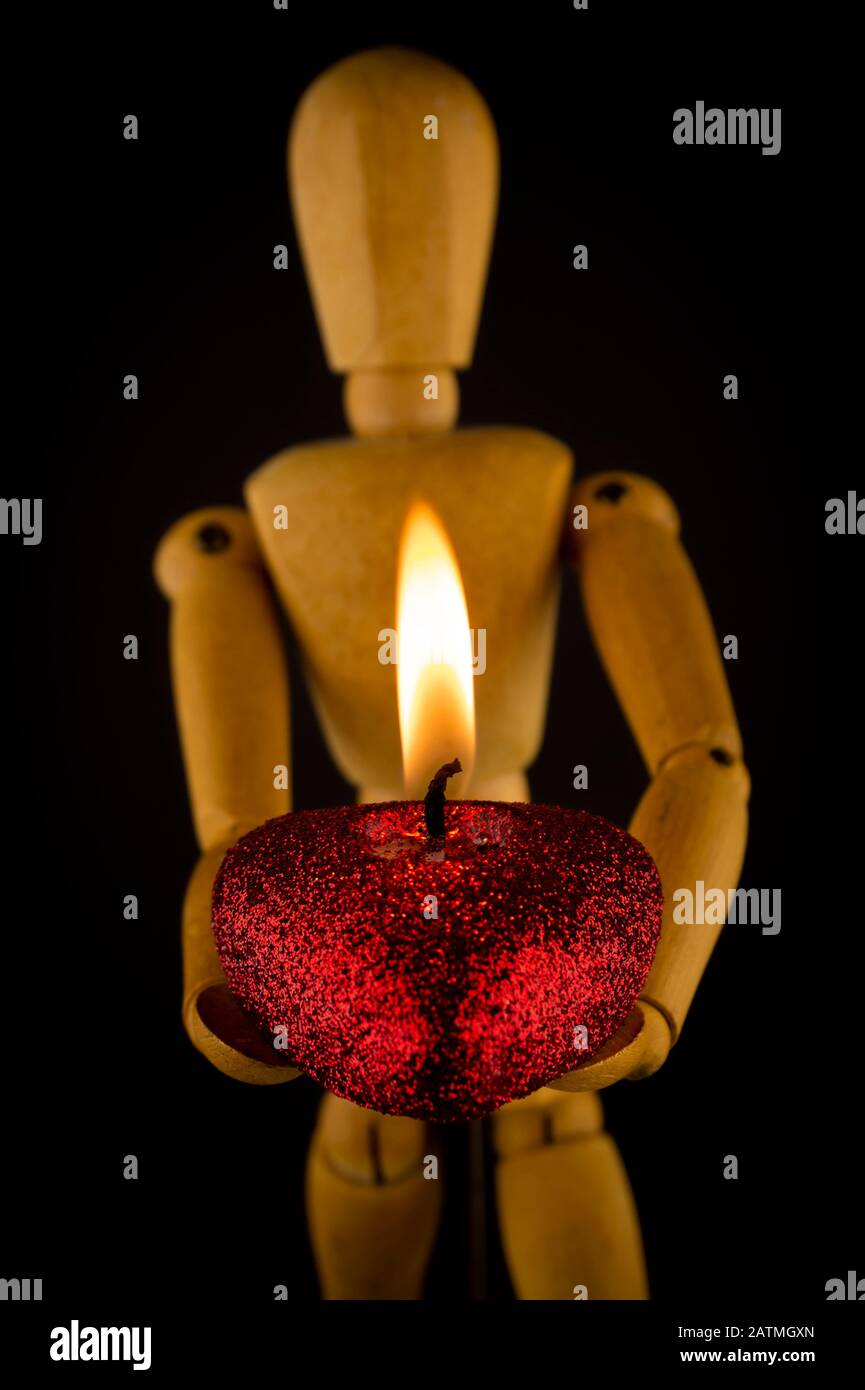 Wooden puppet or figure holding a burning red candle over a dark ...