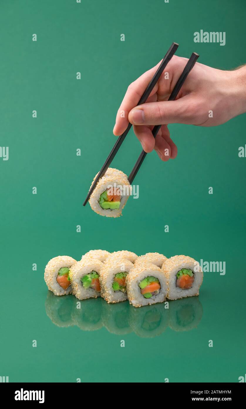 Hand holding sushi roll with chopsticks on green background. set of rolls Stock Photo - Alamy