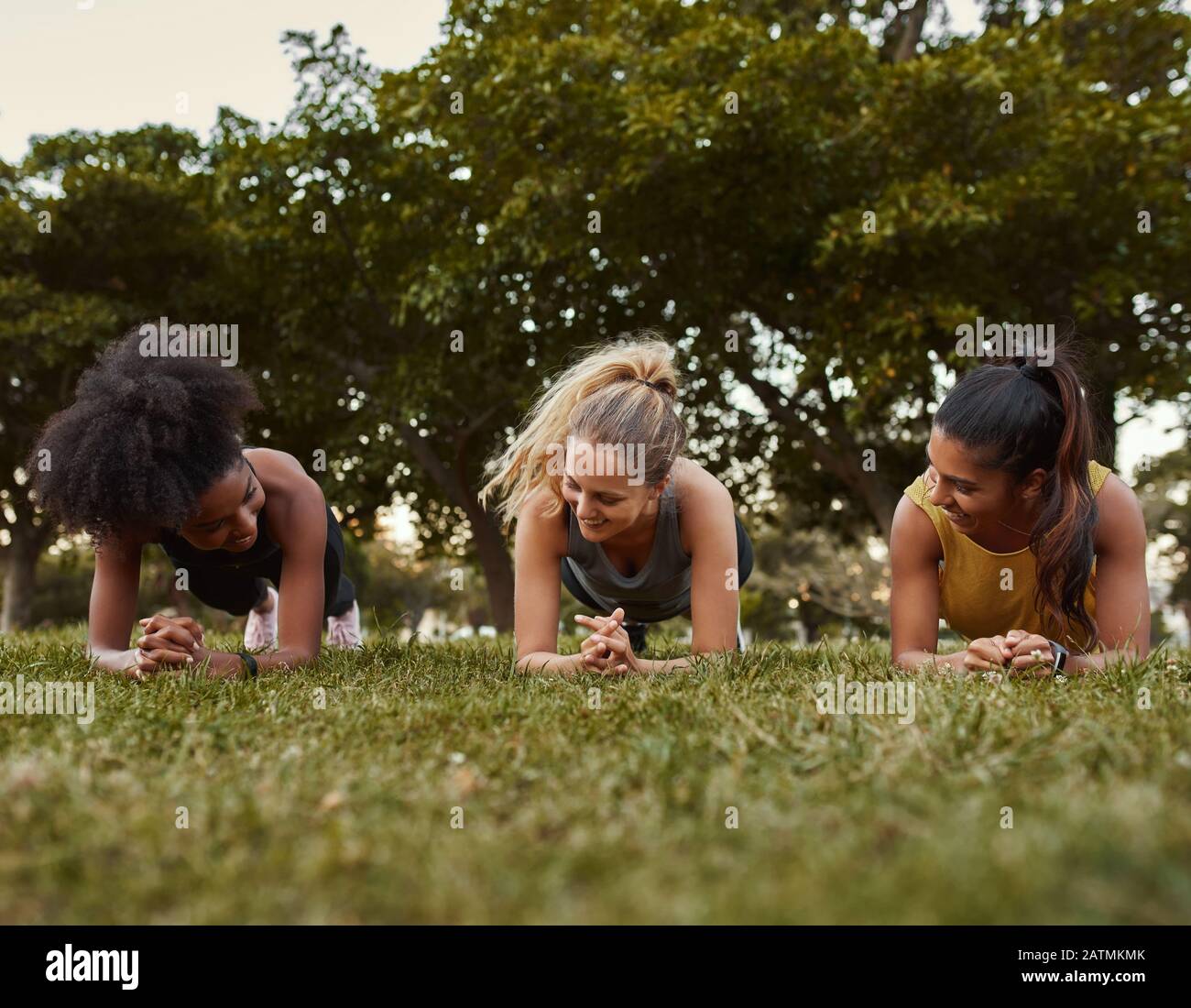 Three multiethnic smiling young active and sporty women doing plank ...