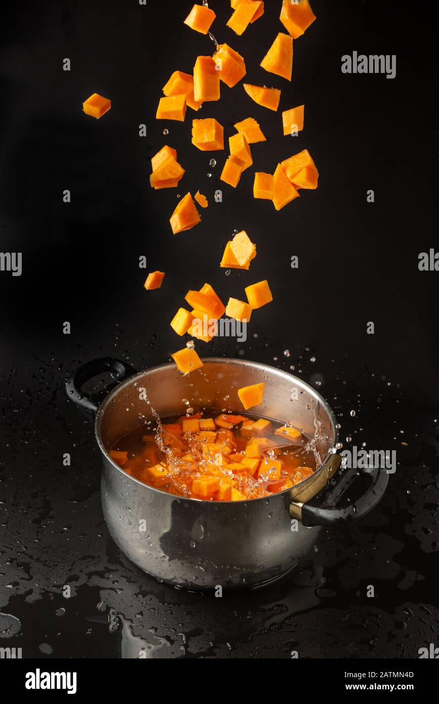 Diced pumpkin falling in a boiling pot, isolated black background with ...