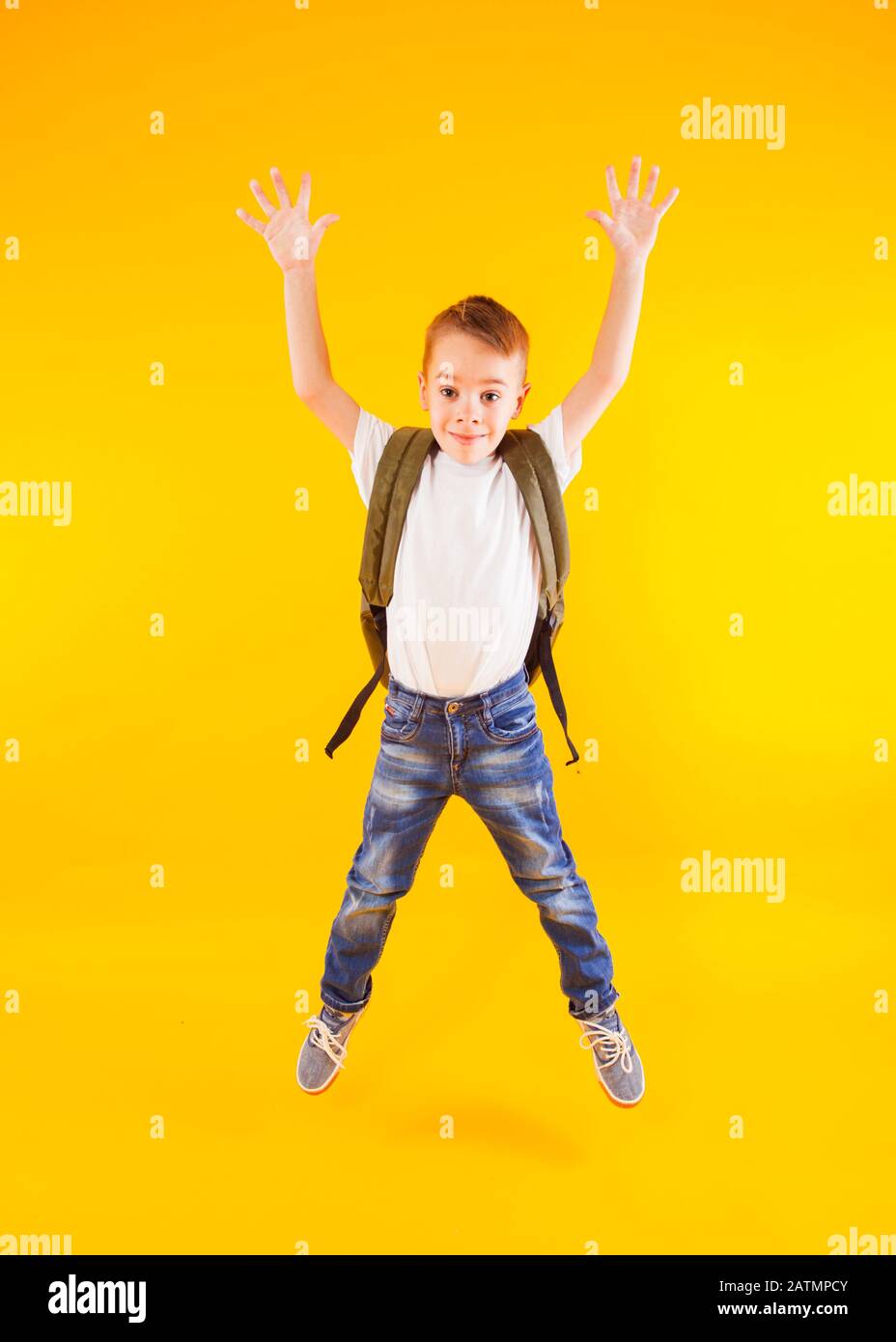 Happy child jumping with backpack over yellow background back to school ...