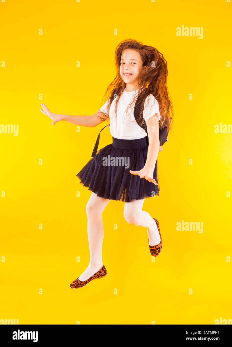 Schoolgirl jumping high over yellow background. Back to school. Happy ...
