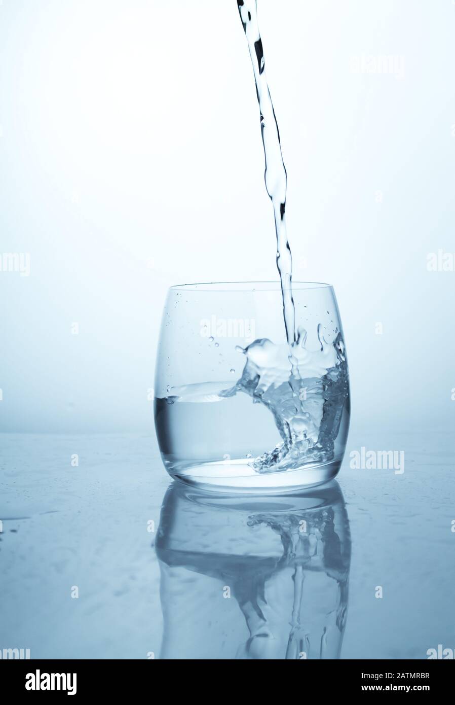 A stream of water flowing into a transparent glass cup with a splash of ...