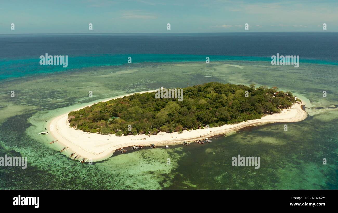 Tropical island and sandy beach surrounded by atoll coral reef and blue ...