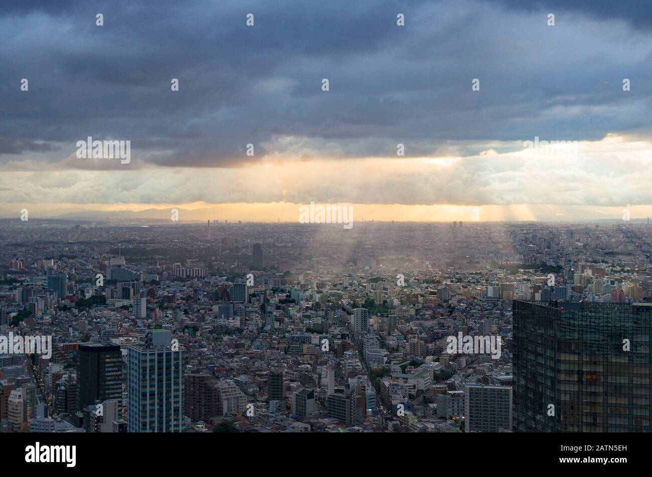 Aerial view of urban sprawl of Tokyo, Shinjuku district with sun rays penetrating dramatic sky ...