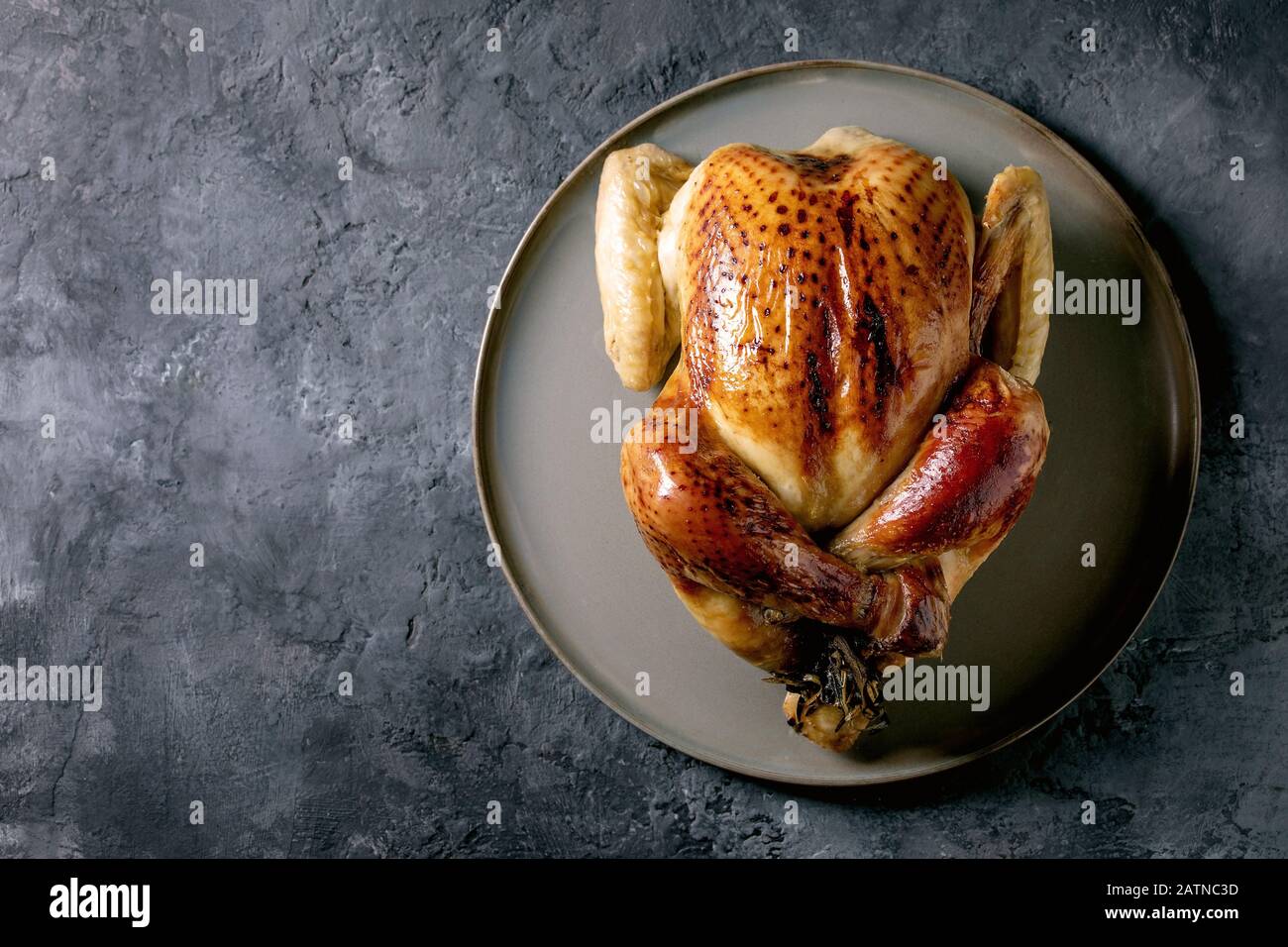 Whole baked chicken poultry on ceramic plate over black concrete ...